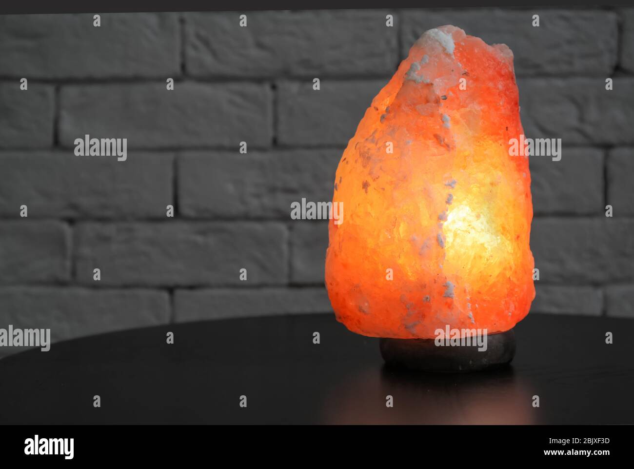 Himalayan salt lamp on table against brick wall background Stock Photo ...