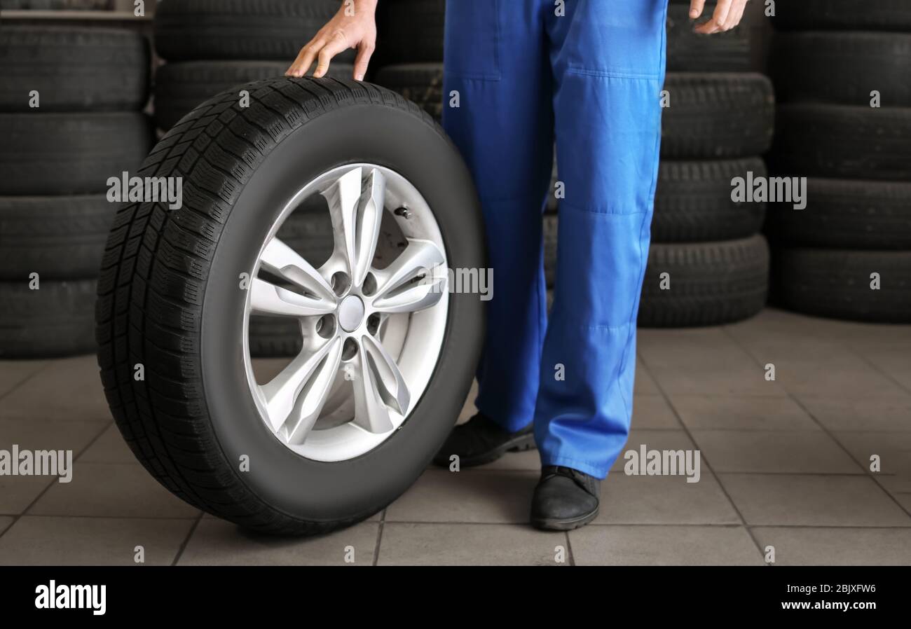 Mechanic with car wheel in repair shop. Tire service Stock Photo - Alamy