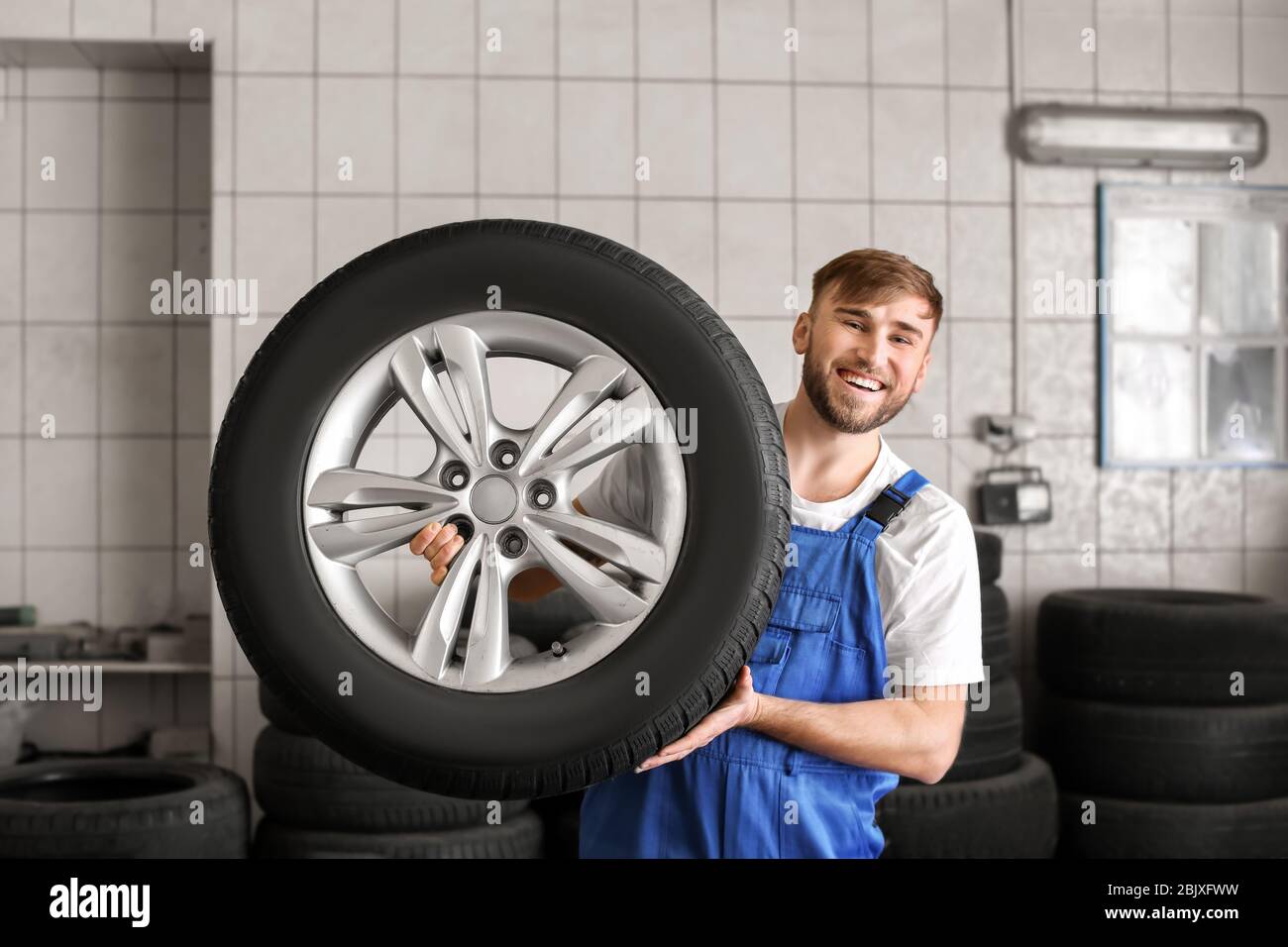 Mechanic with car wheel in repair shop. Tire service Stock Photo - Alamy