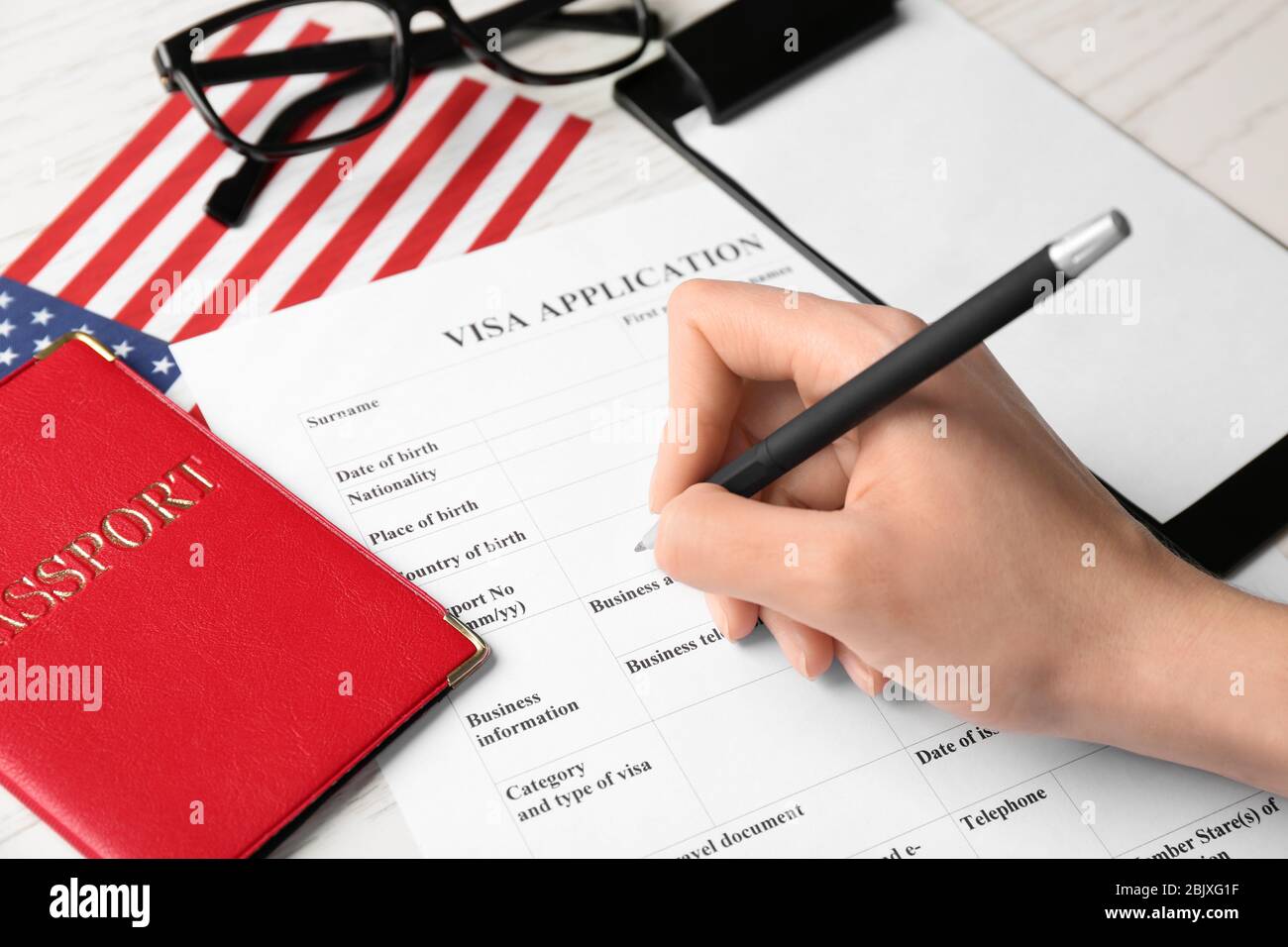 Woman filling visa application form near American flag at table ...