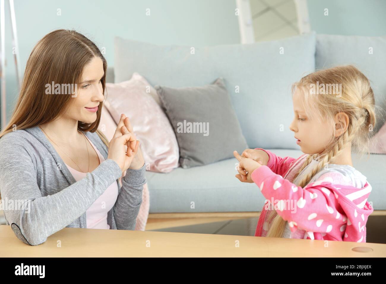 Mother teaching her deaf mute daughter to use sign language at home ...