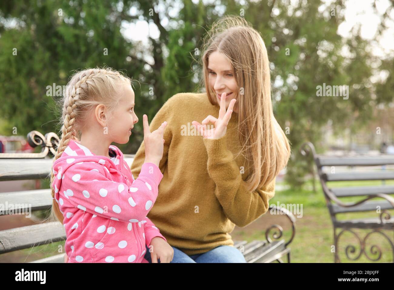 Mother teaching her deaf mute daughter to use sign language outdoors ...