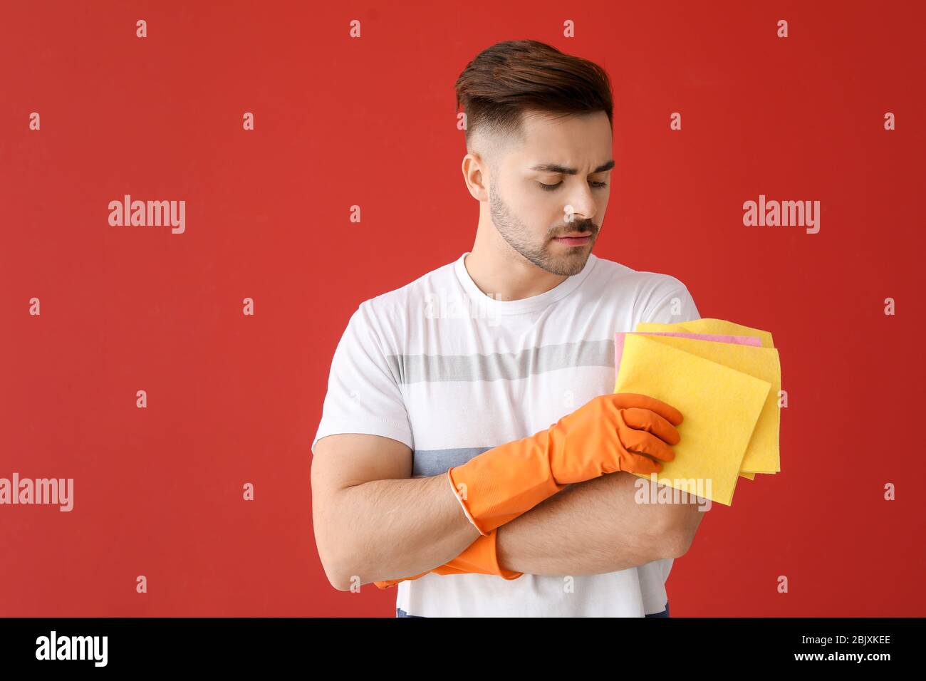 Sad young man with cleaning rags on color background Stock Photo - Alamy