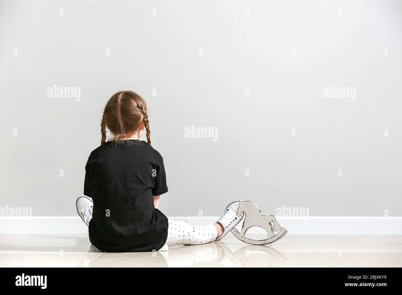 Little girl with autistic disorder sitting on floor near grey wall ...