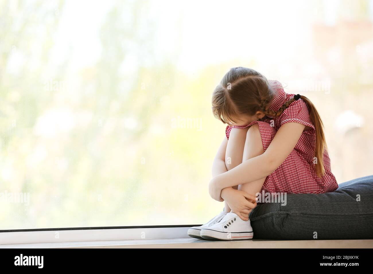 Sad little girl with autistic disorder sitting on window sill at home ...
