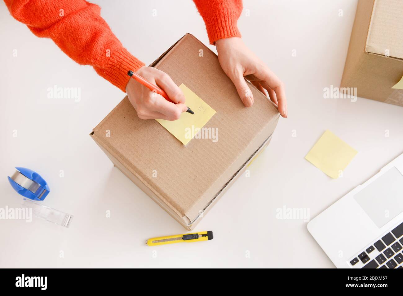 Young woman preparing parcel for client at table Stock Photo - Alamy