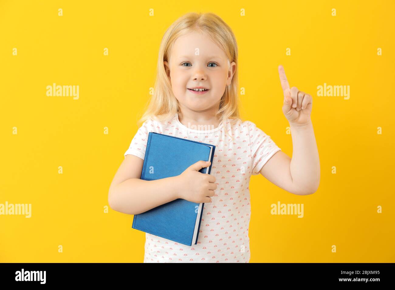 Portrait of adorable little girl with book and raised index finger on ...