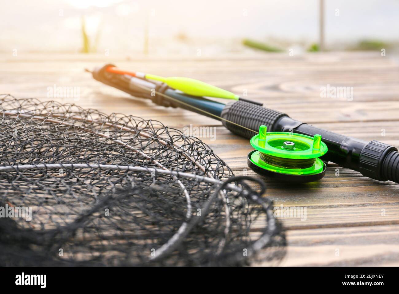 Modern fishing rod with net on pier near river, closeup Stock Photo - Alamy