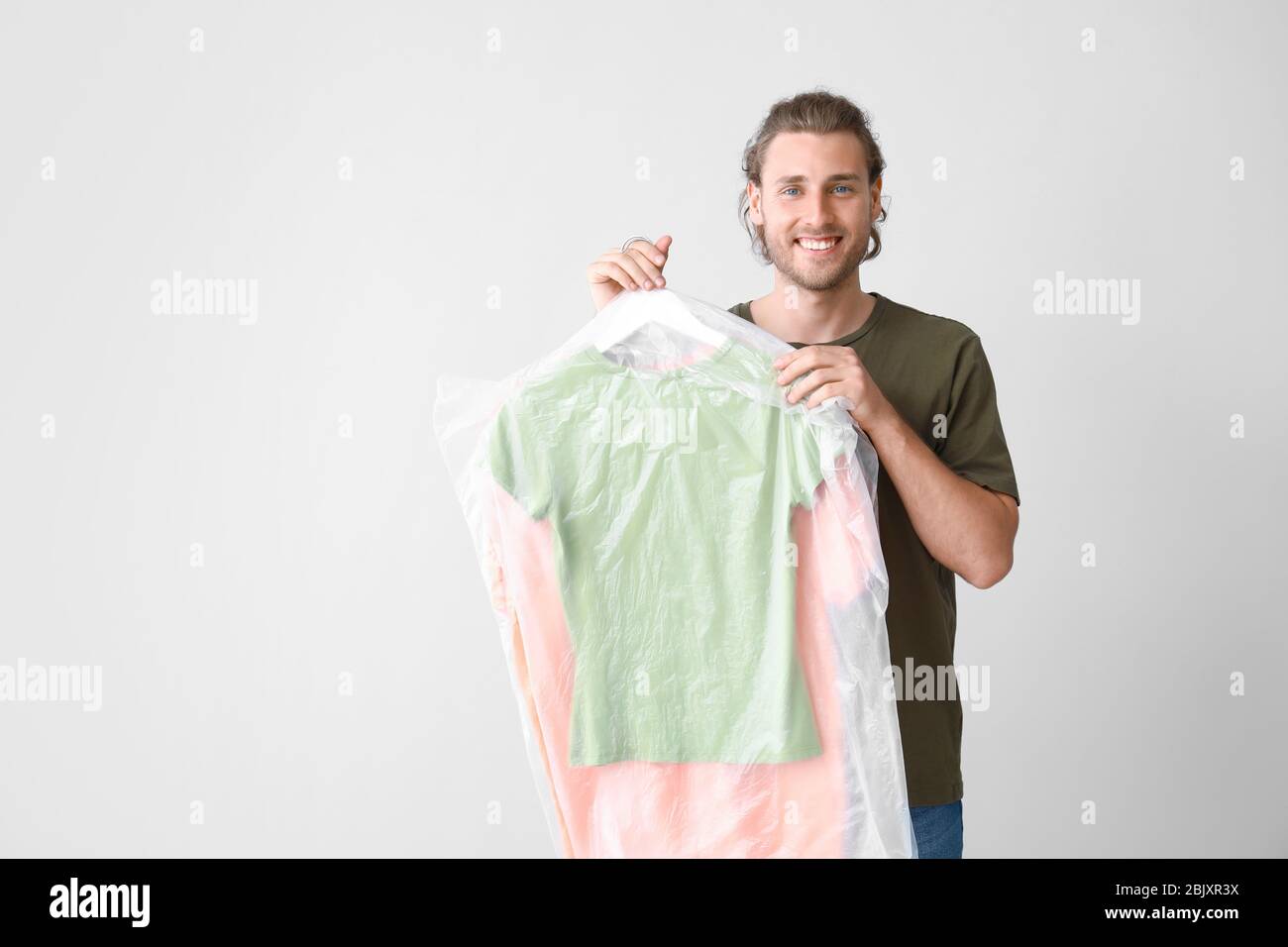 Man with clothes after dry-cleaning on light background Stock Photo - Alamy