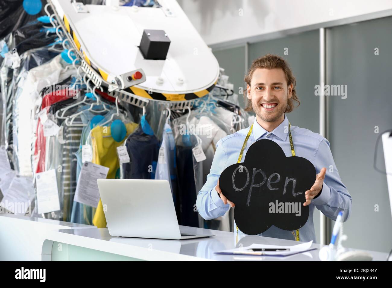 Worker of modern dry-cleaner's holding poster with text OPEN at ...