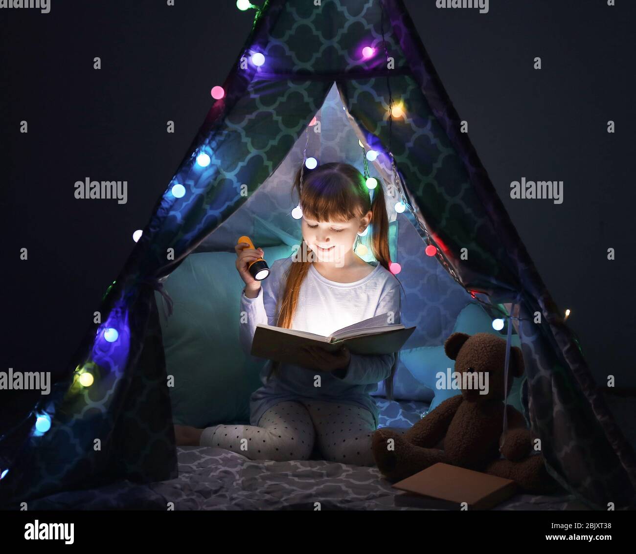 Cute little girl reading book in shelter at night Stock Photo - Alamy
