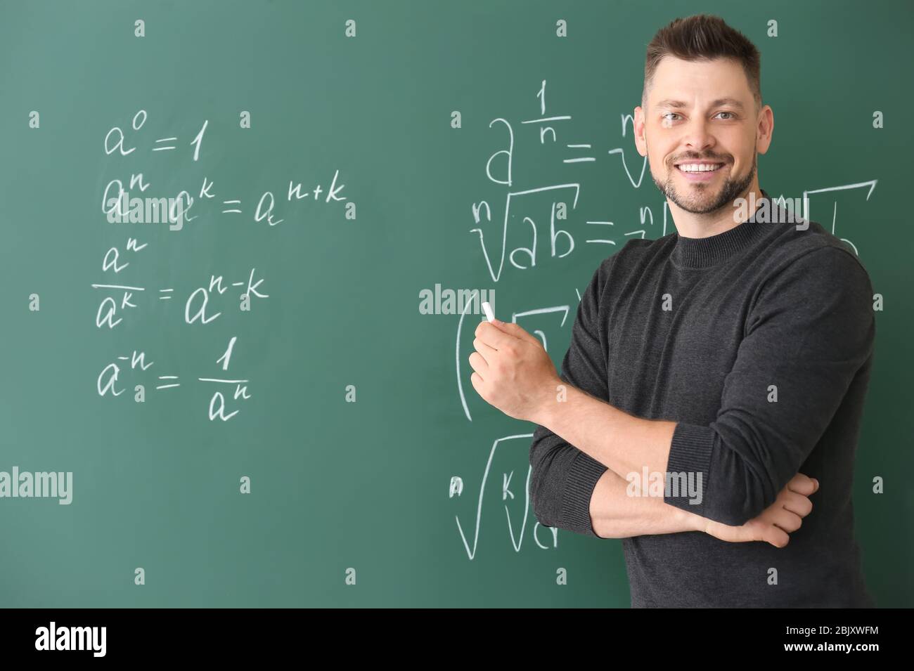 Handsome math teacher writing on blackboard in classroom Stock Photo ...