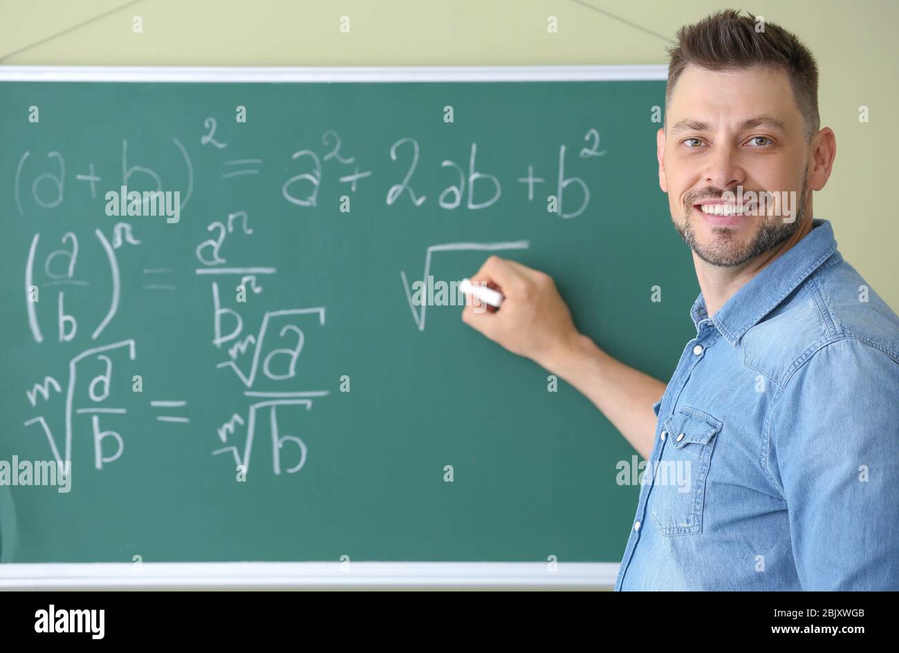 Handsome math teacher writing on blackboard in classroom Stock Photo ...