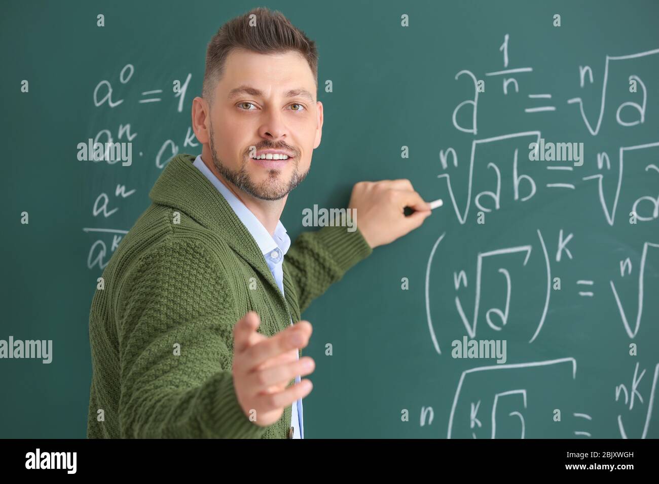 Handsome math teacher writing on blackboard in classroom Stock Photo ...