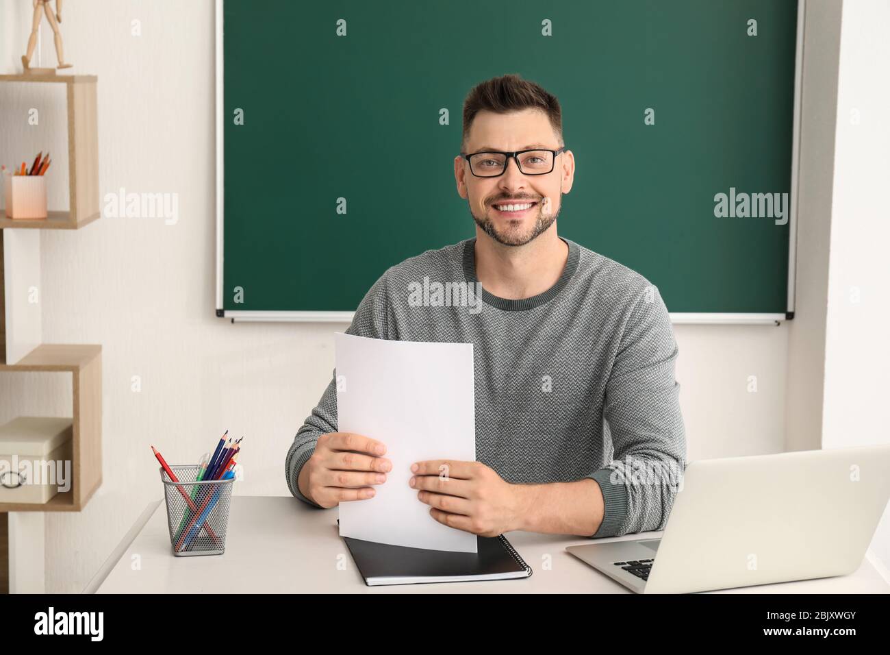 Handsome male teacher sitting at table in classroom Stock Photo - Alamy