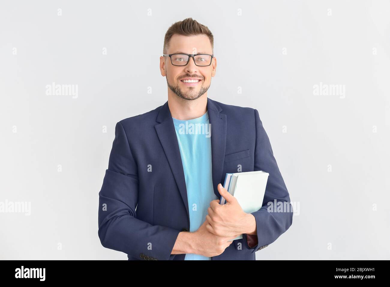 Handsome male teacher with books on light background Stock Photo - Alamy