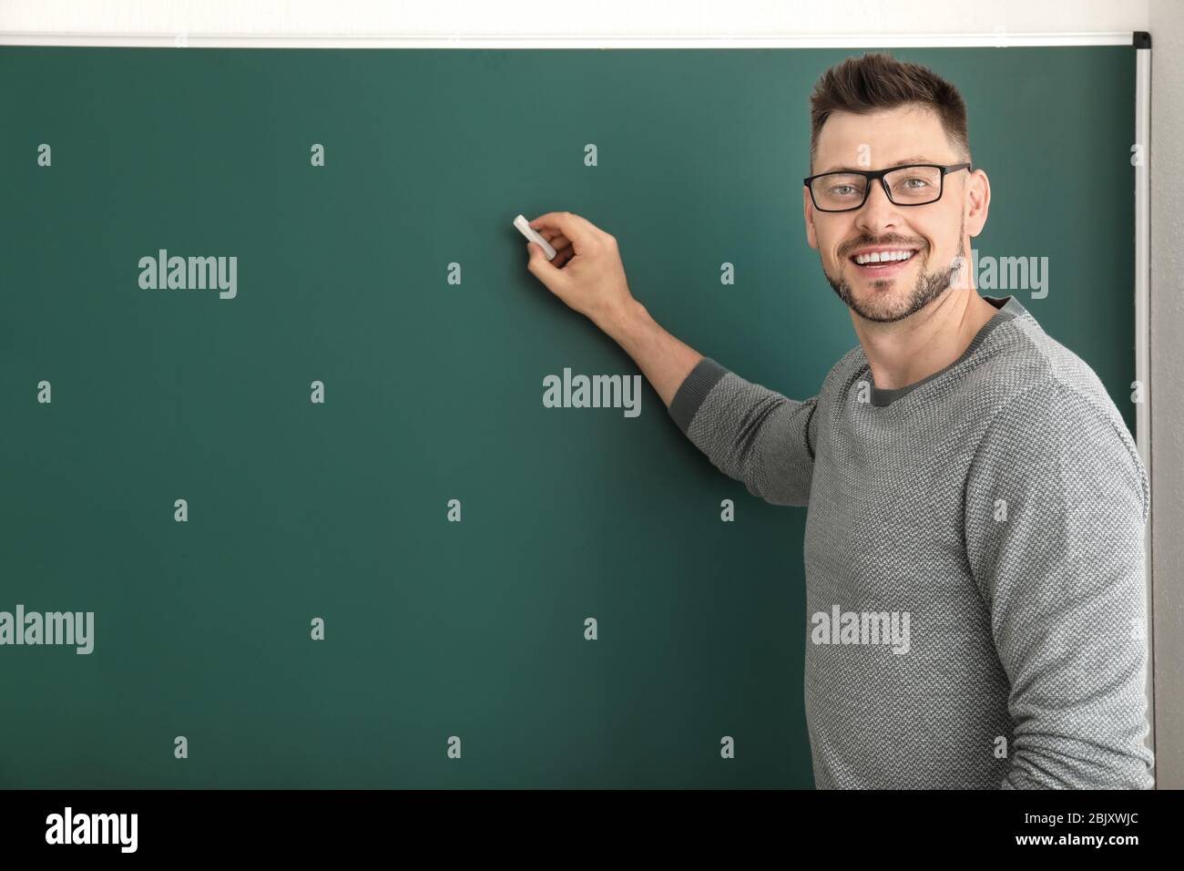 Male teacher writing on blackboard in classroom Stock Photo - Alamy