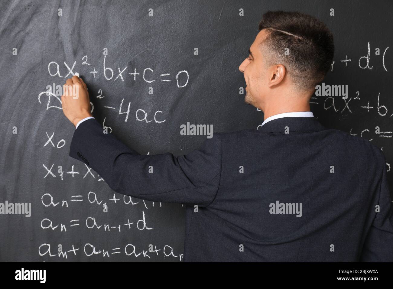 Handsome math teacher writing on blackboard in classroom Stock Photo ...