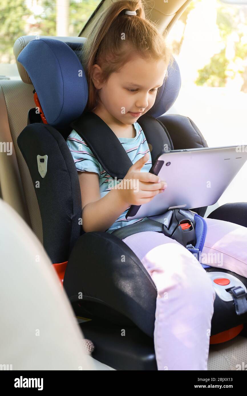 Little girl with tablet computer buckled in car safety seat Stock Photo ...