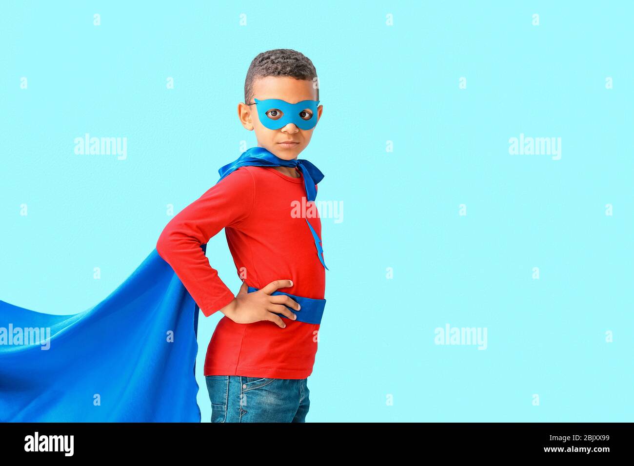 Cute African-American boy dressed as superhero on color background ...