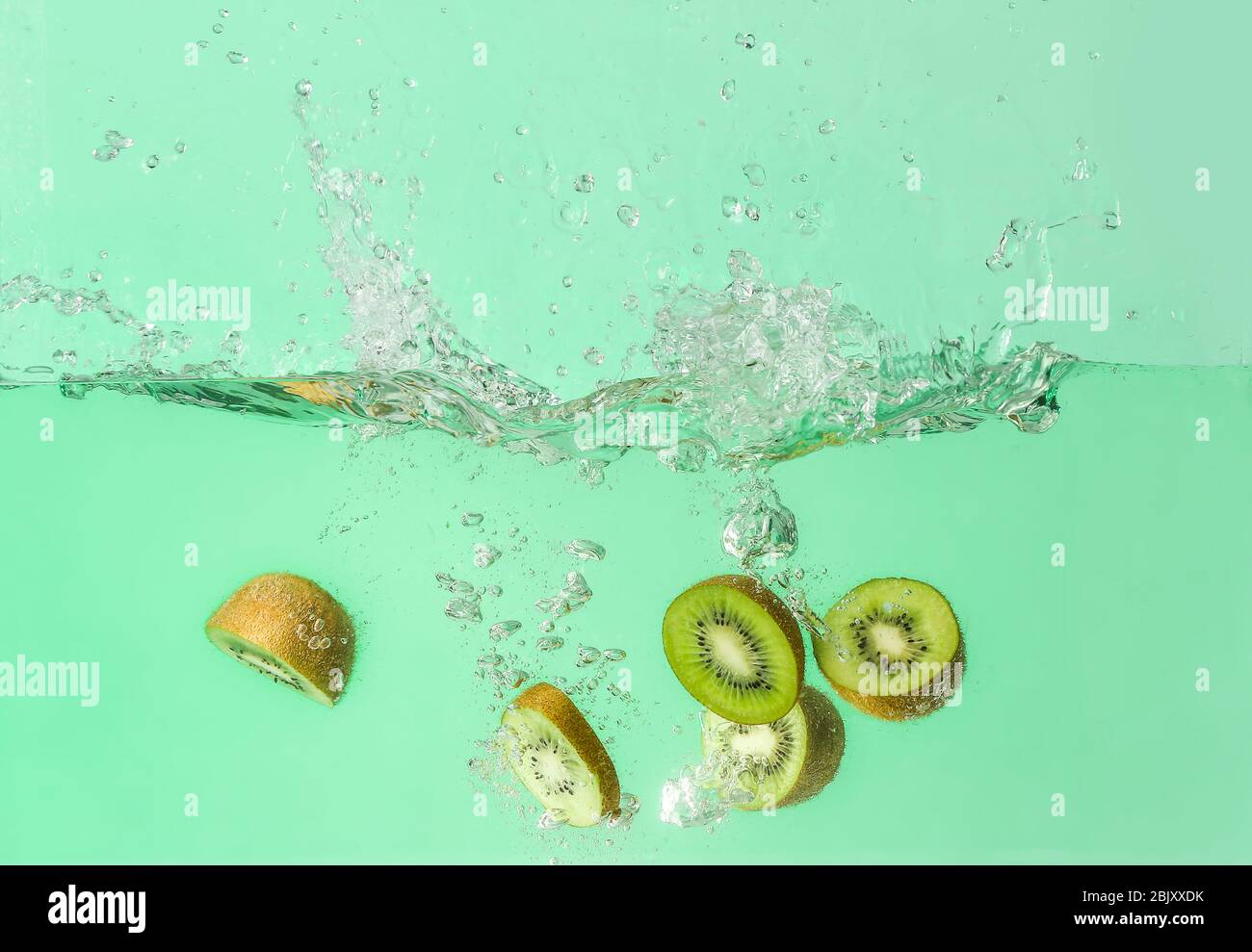 Falling of cut kiwi into water on color background Stock Photo - Alamy