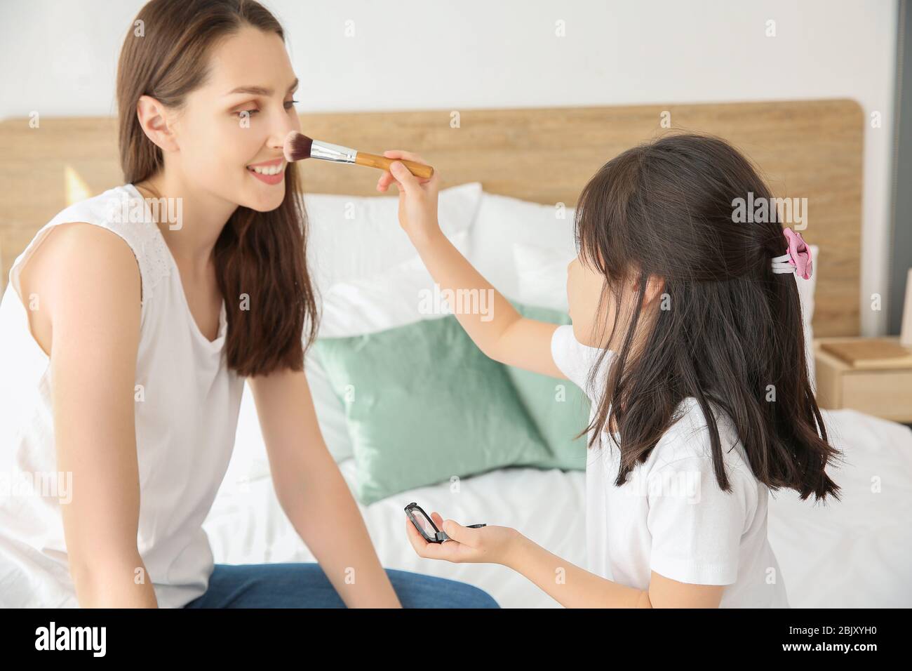 Little girl applying powder onto face of her mother in bedroom Stock ...