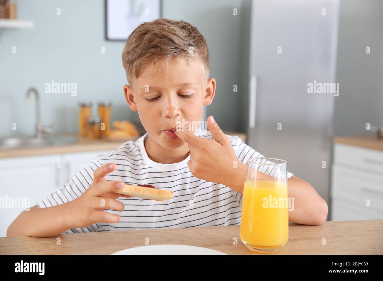 Funny little boy eating tasty toasts with jam in kitchen Stock Photo ...
