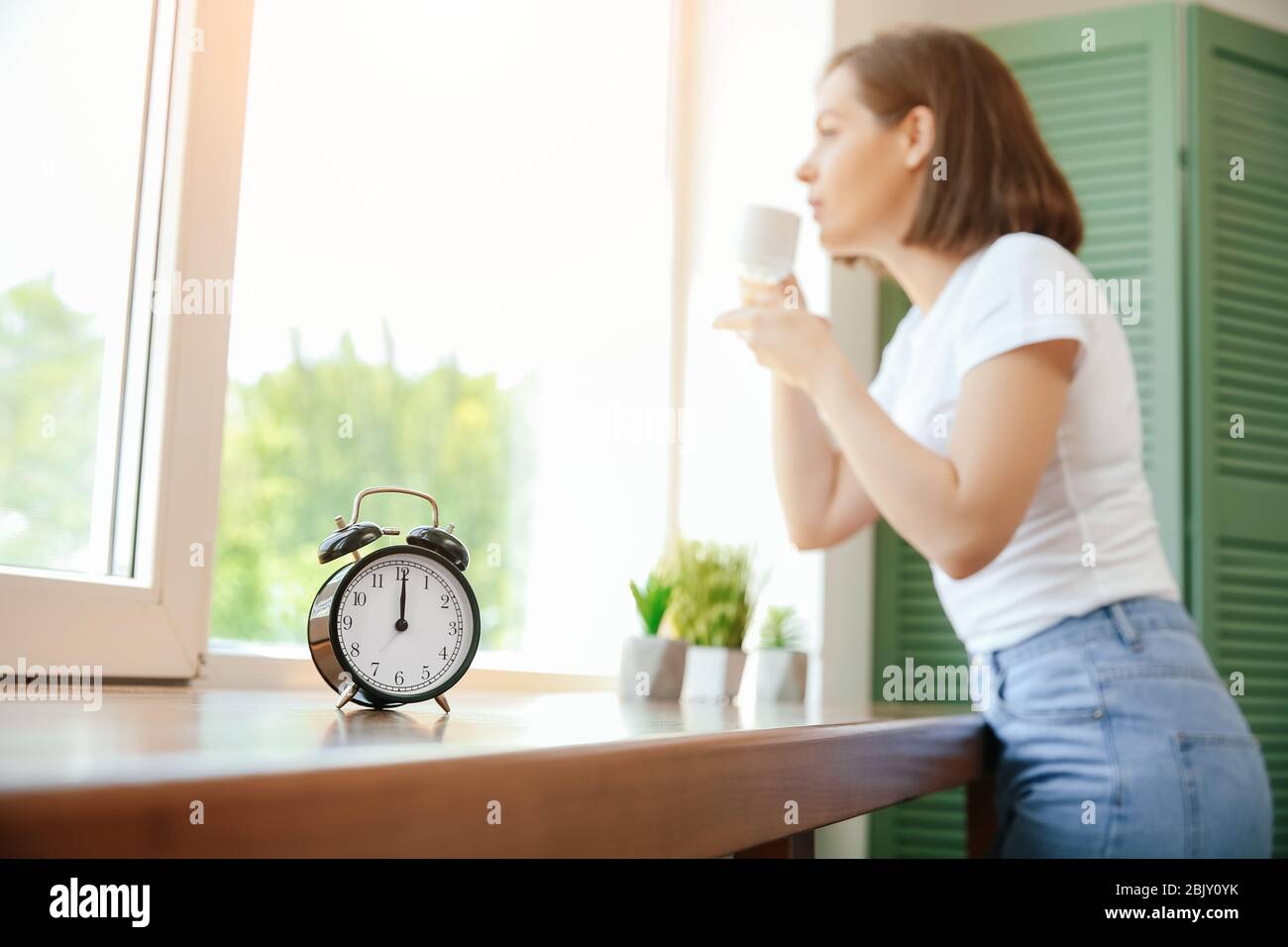 Clock on window sill of beautiful young woman drinking coffee Stock ...