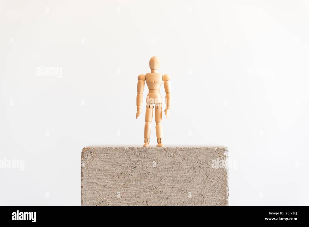 Wooden human figure standing isolated on a concrete block. Symbol of ...
