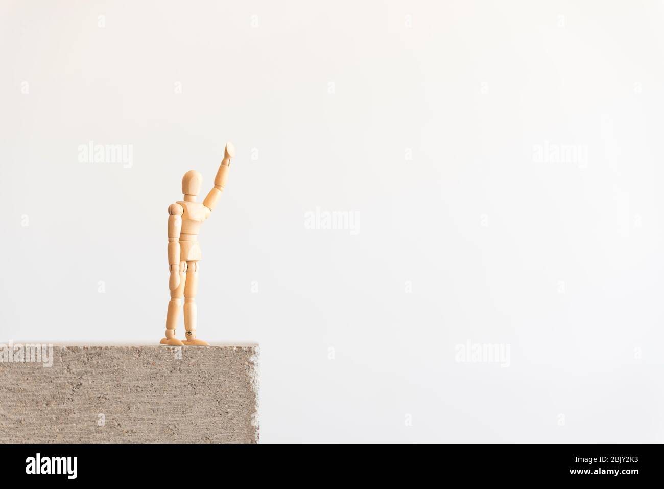 Wooden human figure standing isolated on a concrete block, waving with ...