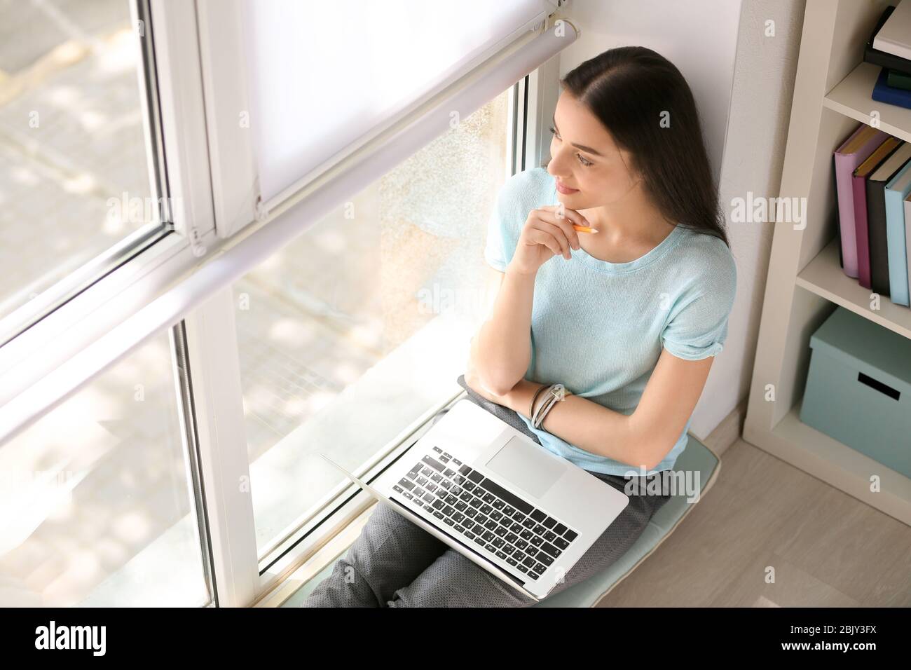 Female student with laptop preparing for exam near window Stock Photo ...