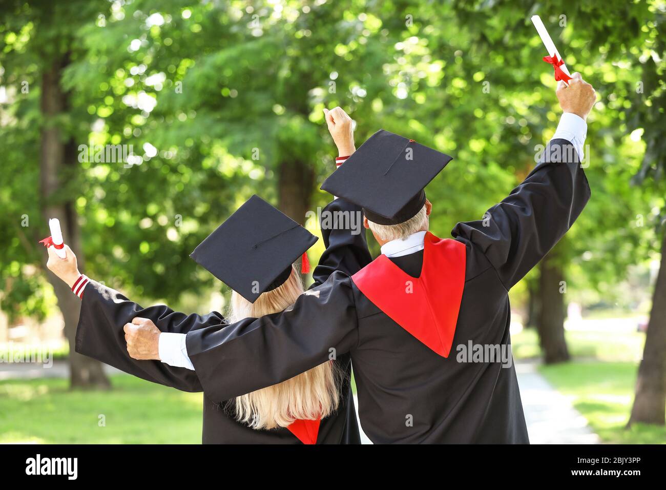 Happy mature couple in bachelor robes outdoors, back view Stock Photo ...