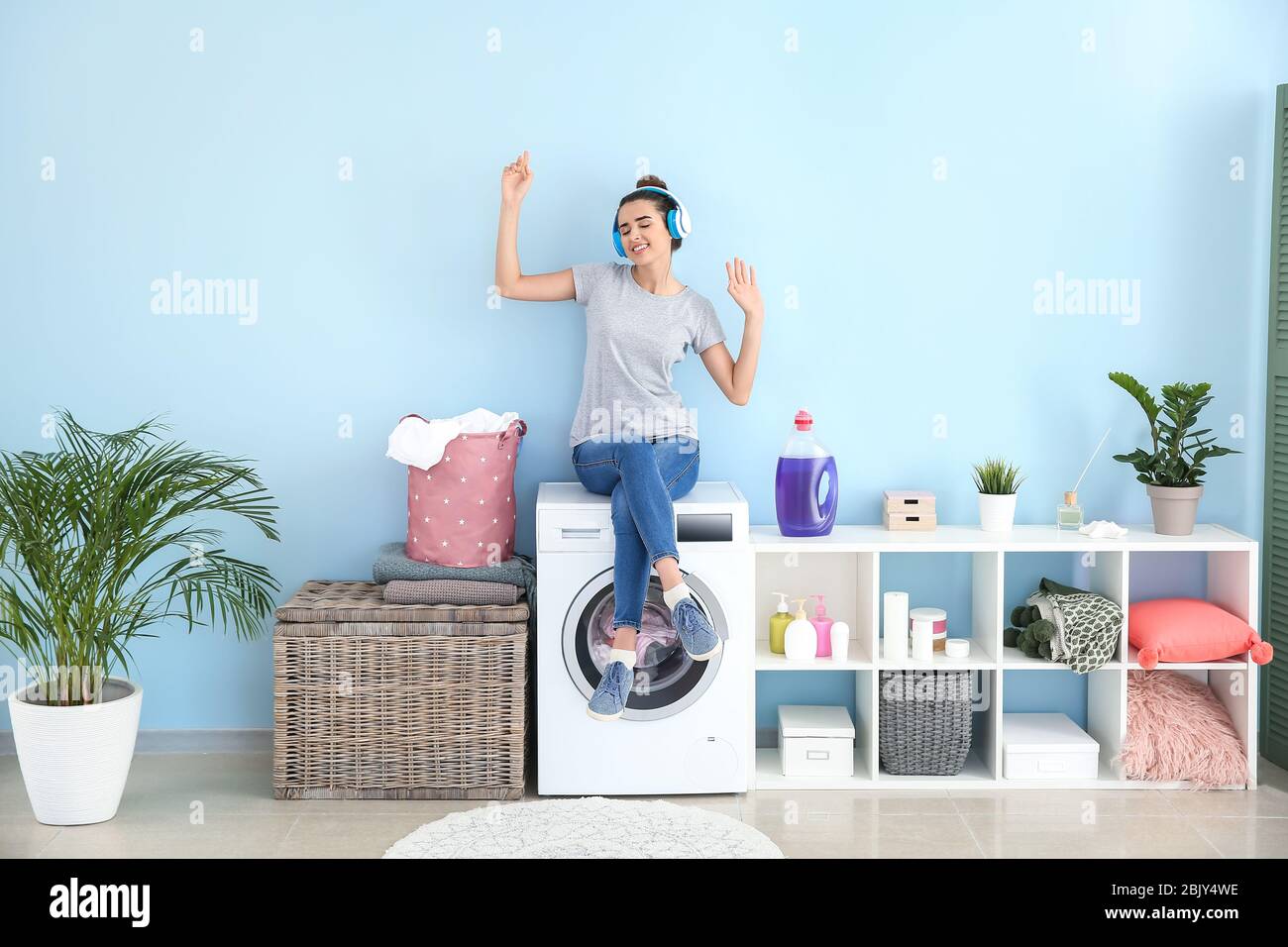 Beautiful young woman listening to music while doing laundry at home ...