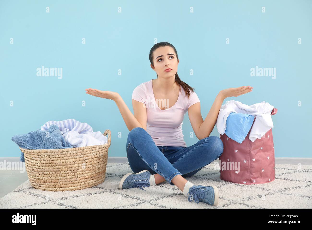 Upset young woman with laundry sitting on floor near color wall Stock ...