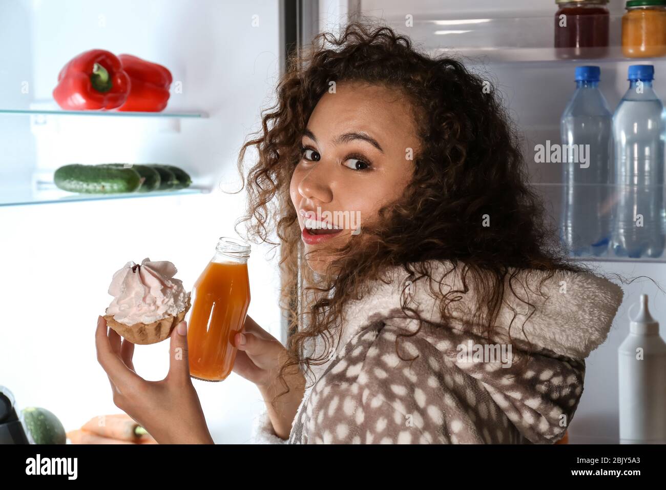 Afraid woman caught in the act of eating tasty cake near refrigerator ...