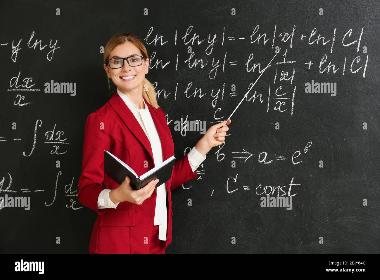 Beautiful math teacher with book and pointer near blackboard in ...
