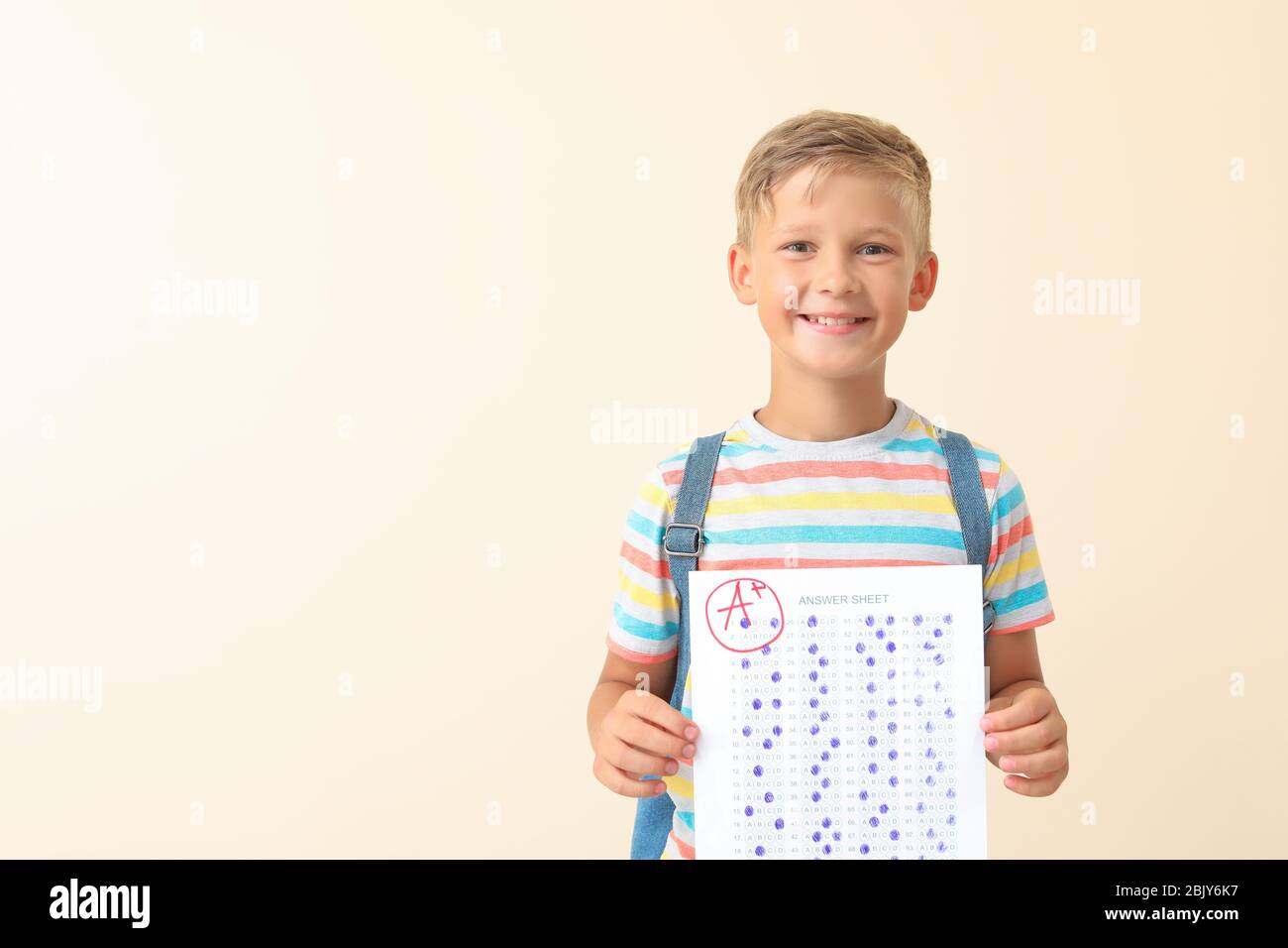 Happy boy with answer sheet for school test on light background Stock ...