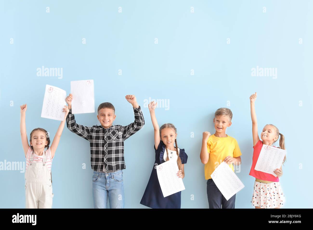 Happy children with answer sheets for school test on light color ...