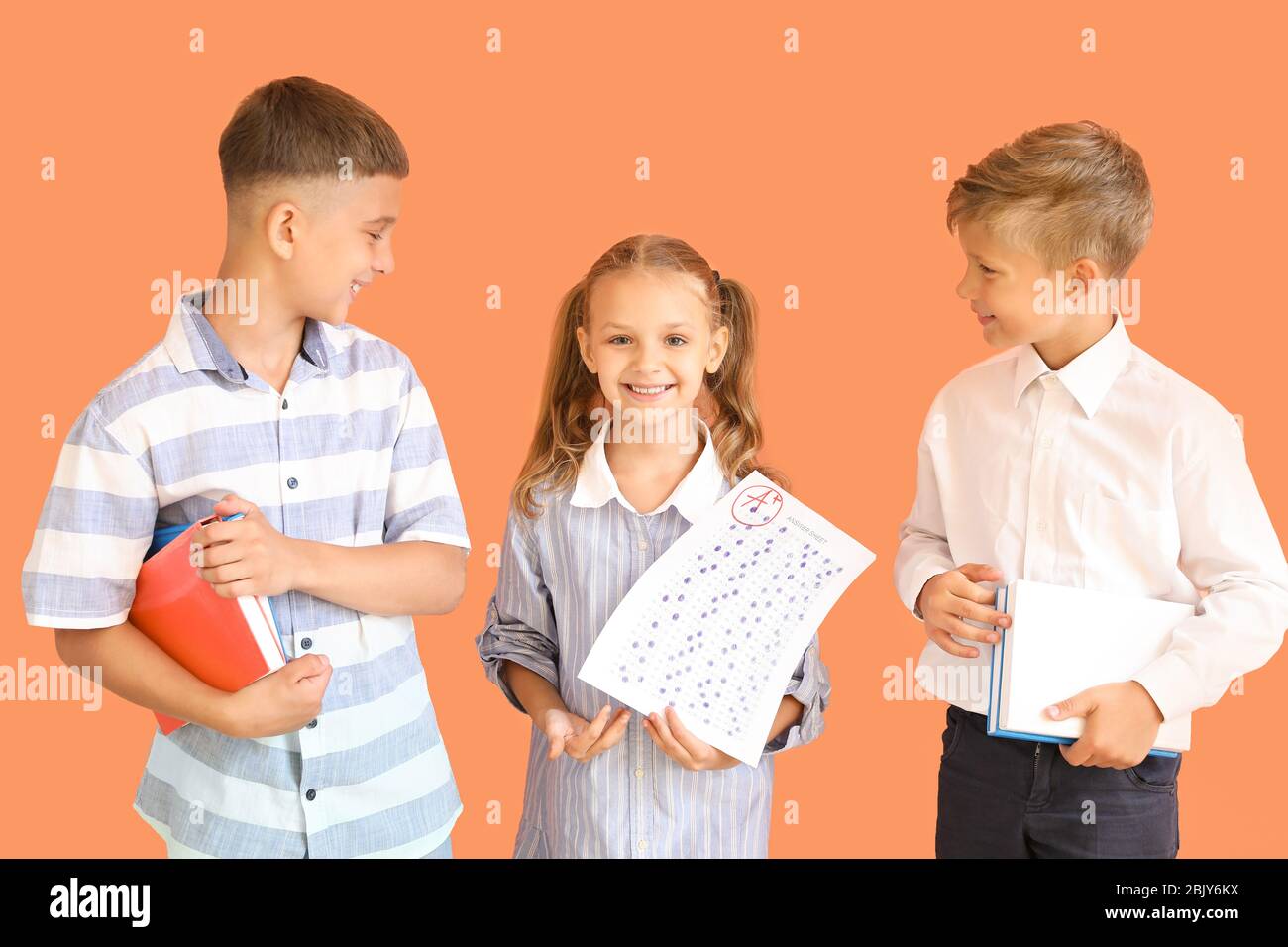 Happy children with answer sheet for school test on color background ...