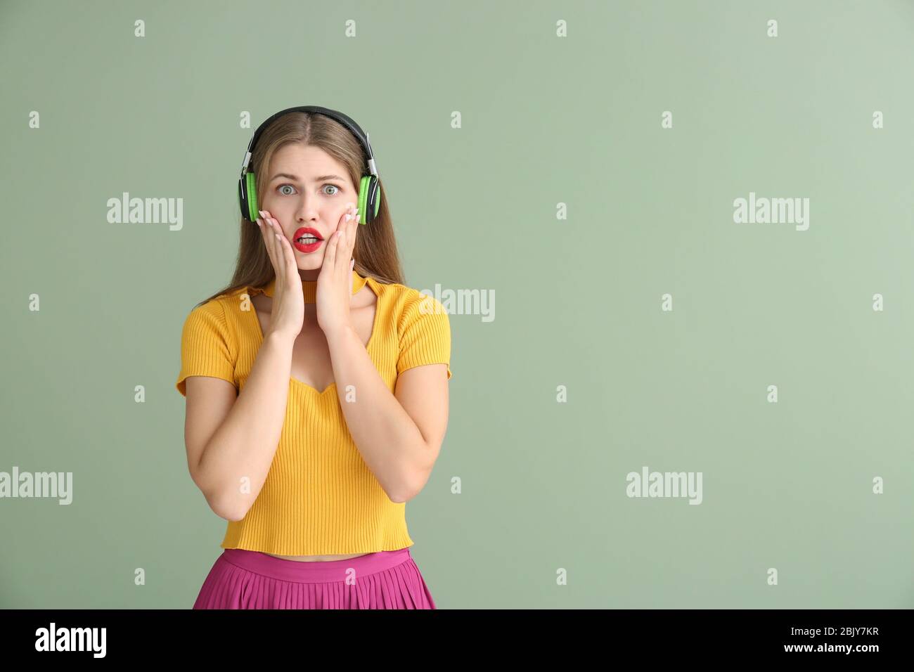 Shocked young woman listening to music on color background Stock Photo ...