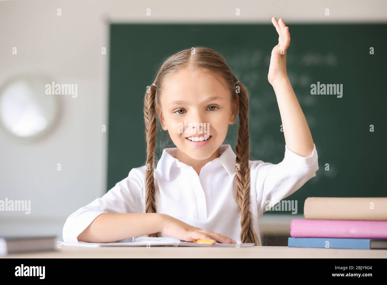 Cute little girl raising hand during lesson in classroom Stock Photo ...