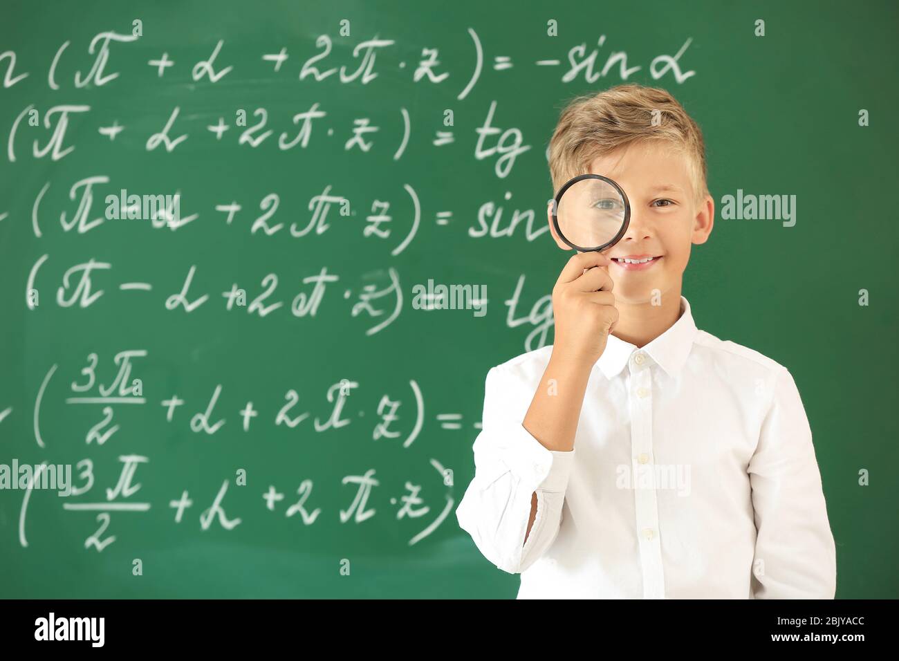 Little boy with magnifying glass near school blackboard in classroom ...