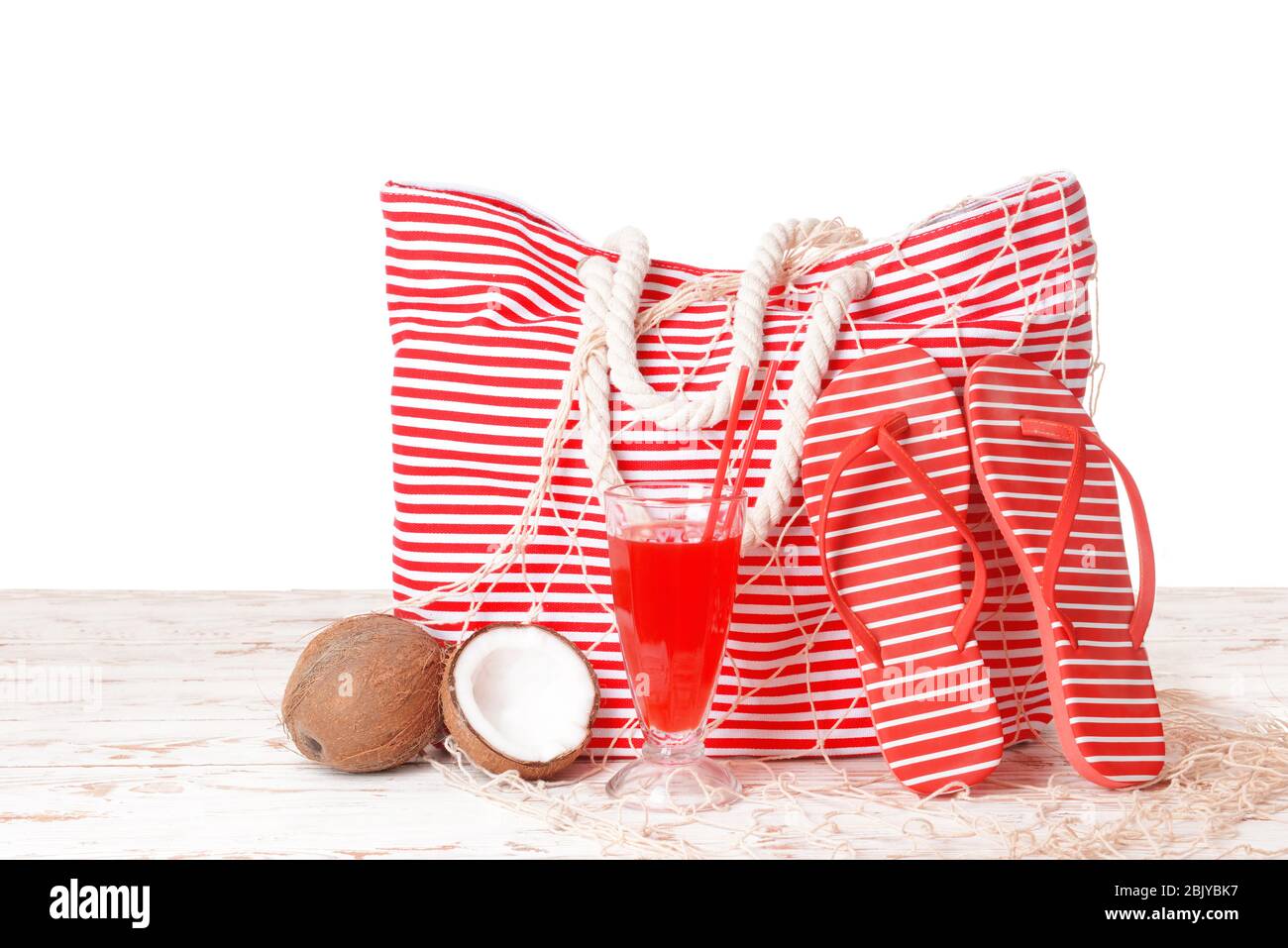 Beach bag, cocktail and accessories on table against white background ...