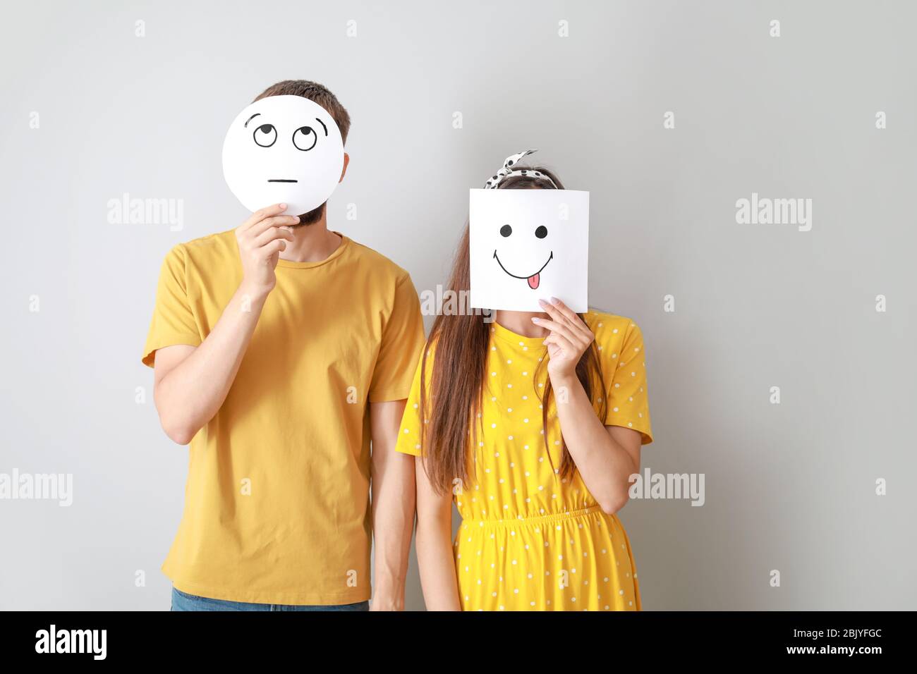Couple hiding faces behind sheets of paper with drawn emoticons on grey ...