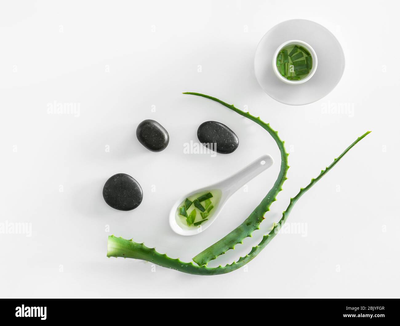 Fresh aloe vera leaves with juice and spa stones on white background ...