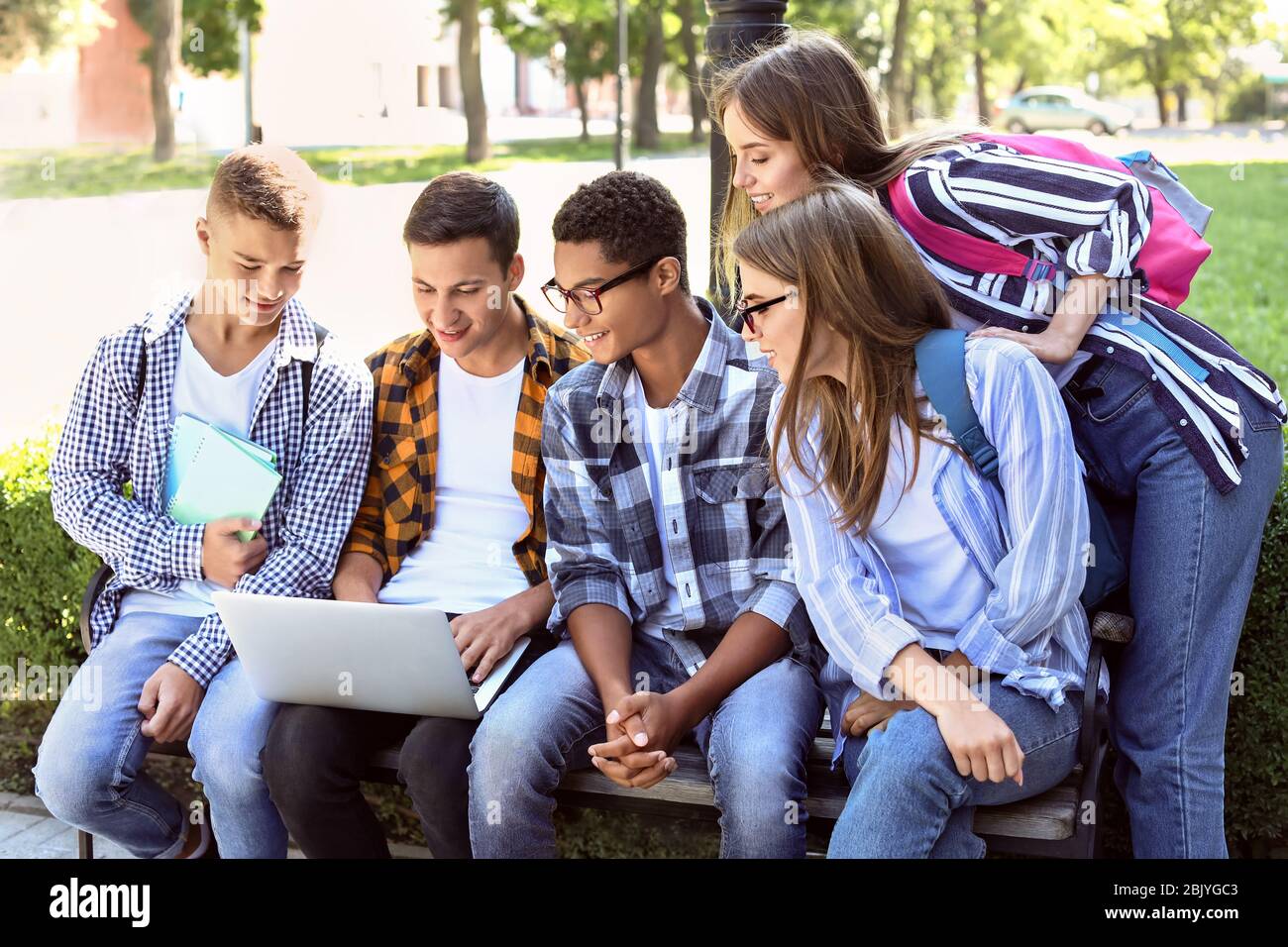 Young students with laptop sitting on bench outdoors Stock Photo - Alamy