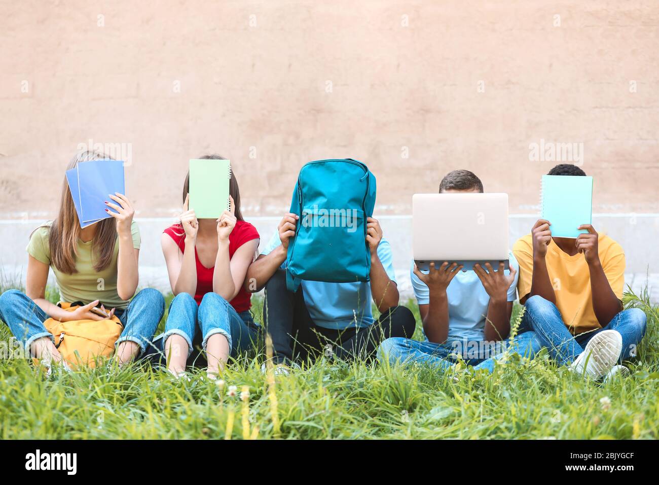 Young students hiding faces while sitting on grass outdoors Stock Photo ...