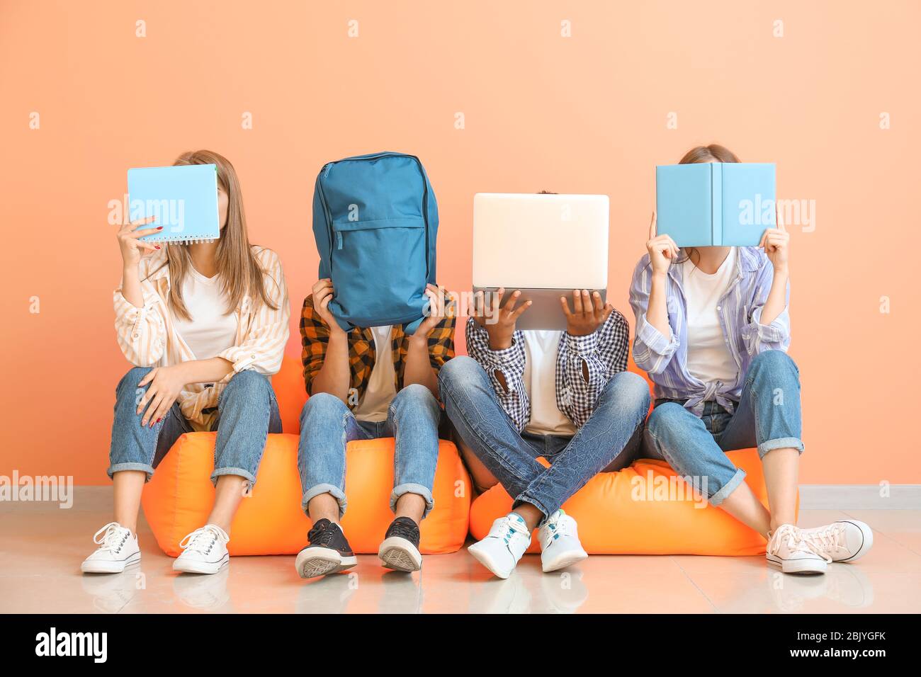 Young students hiding faces while sitting near color wall Stock Photo ...