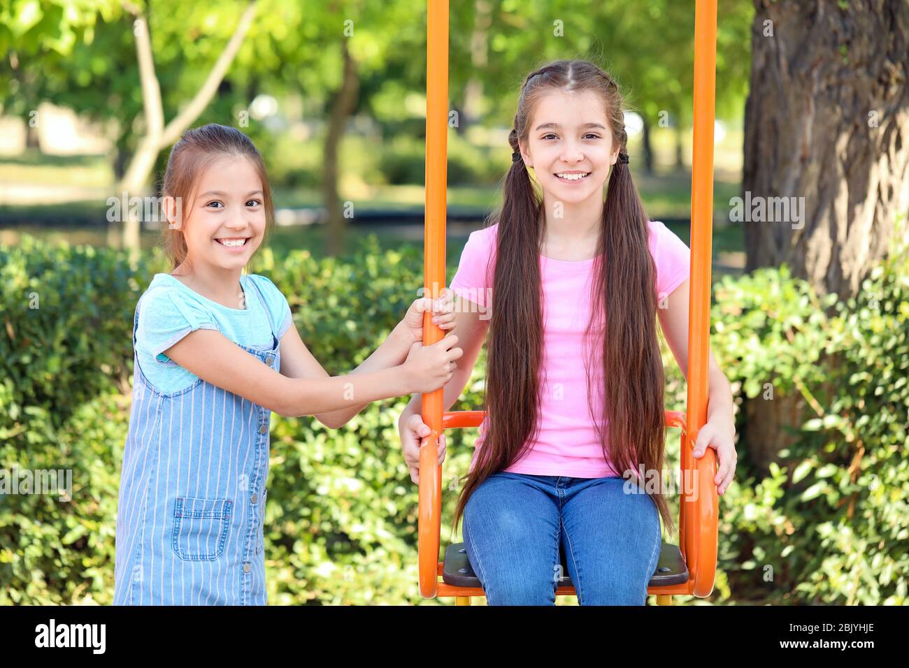 Cute little girls playing on swings in park Stock Photo - Alamy