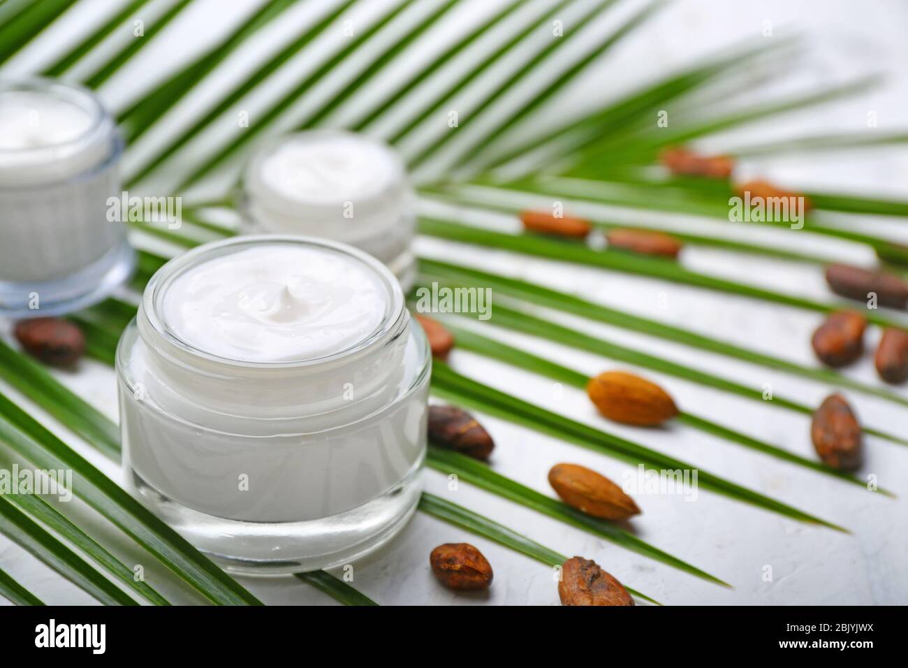 Jars of body cream, palm leaf and almonds on white background Stock ...